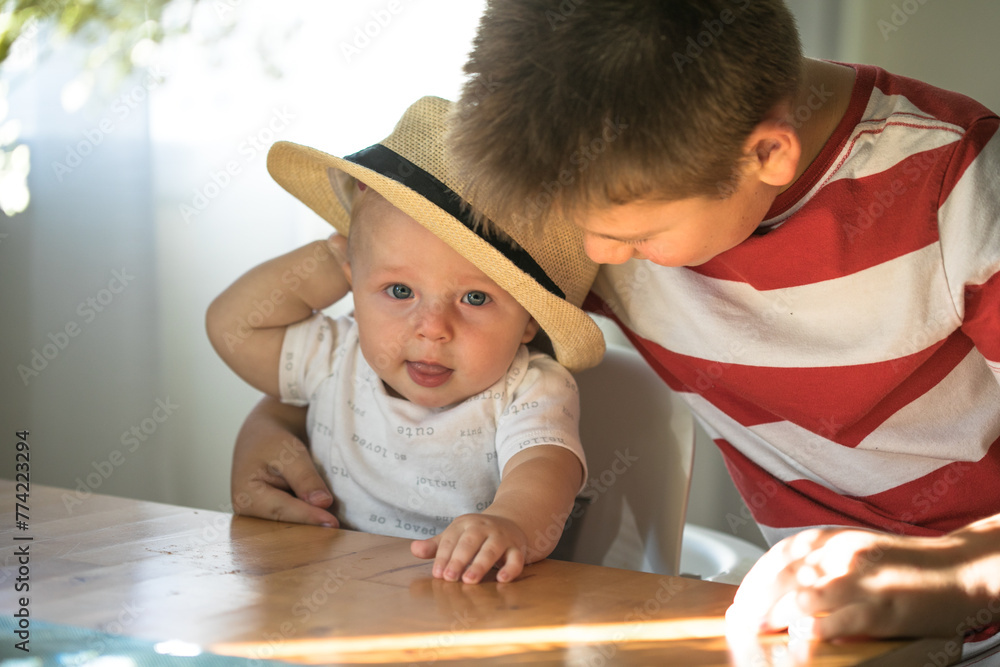 Older brother wearing hat to younger baby brother. Concept siblings and ...