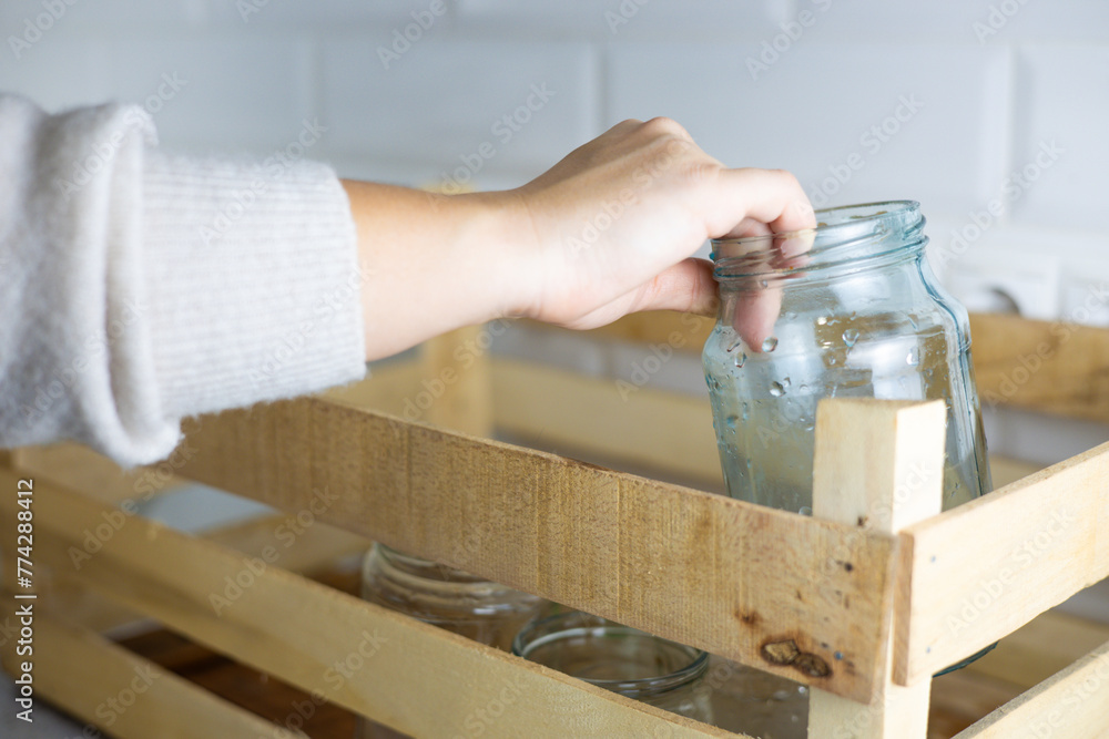 In the kitchen, a woman packs glass jars into a recycling box. A woman ...