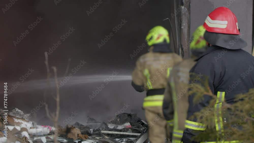 A fireman in helmet and safety uniform extinguishing the fire with hose ...