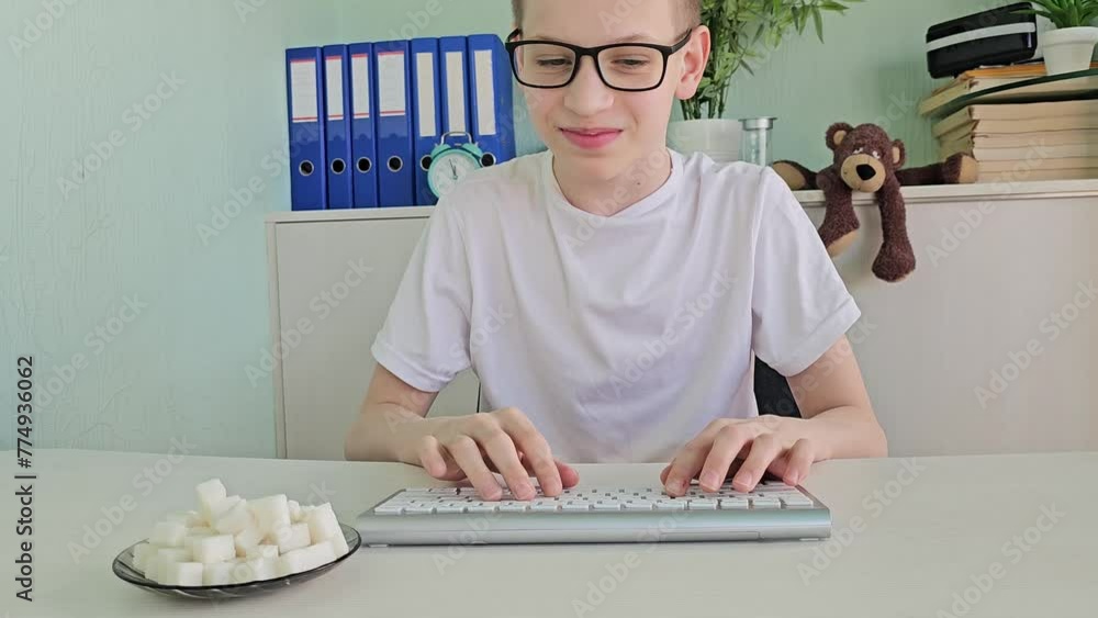 Teenager guy eats sugar while working at the computer at home. Sweet addiction, uncontrolled ...