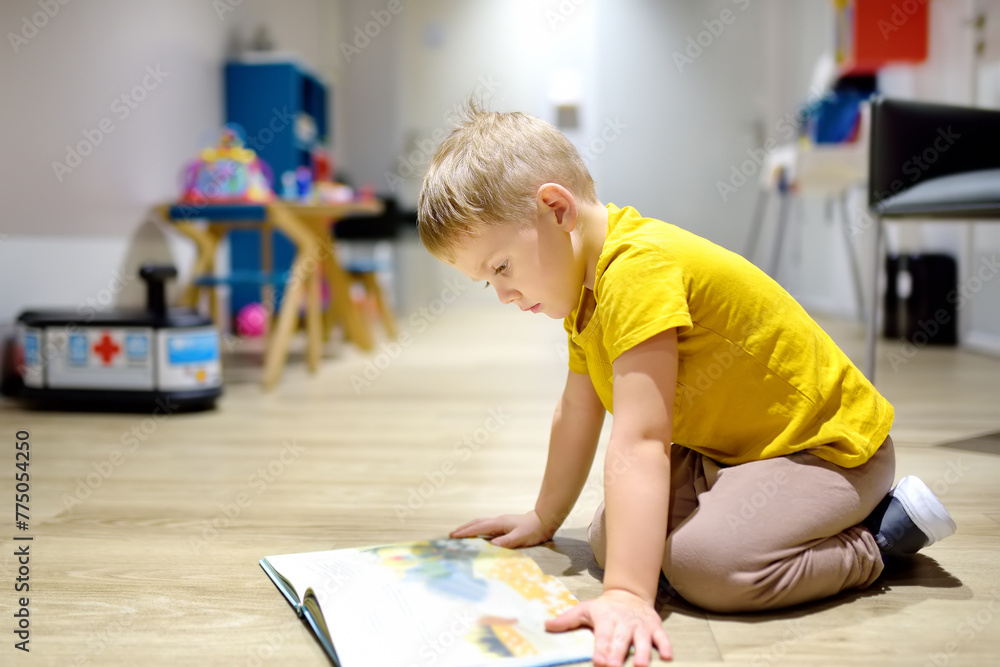 Cute little boy reading a book on the floor in a kindergarten. The ...