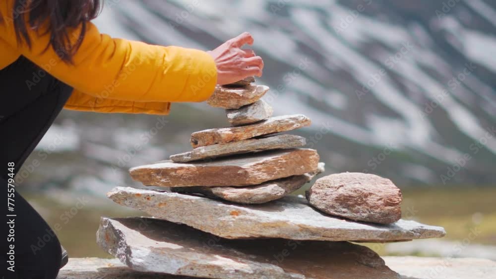Hand of girl builds a balancing stone pile in the snowy mountains at ...