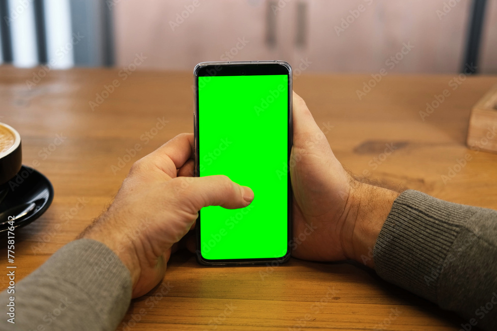 Young man sitting at cafe holding smartphone green mock-up screen in ...