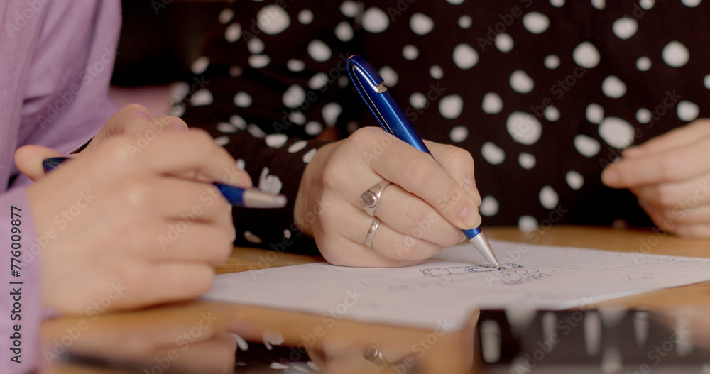 Close-up teacher explains task to student, draws with pen on paper ...