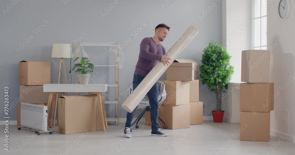 Young happy excited man moving into his new apartment standing among many cardboard boxes and ...