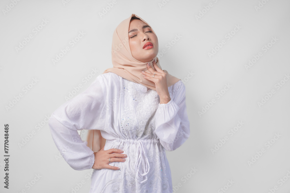 Tired Asian Muslim woman in white dress and hijab holding her neck ...