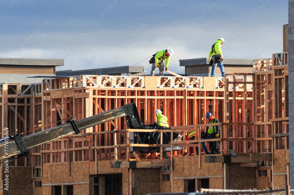 A crew of construction workers atop wooden structures, building a multi ...