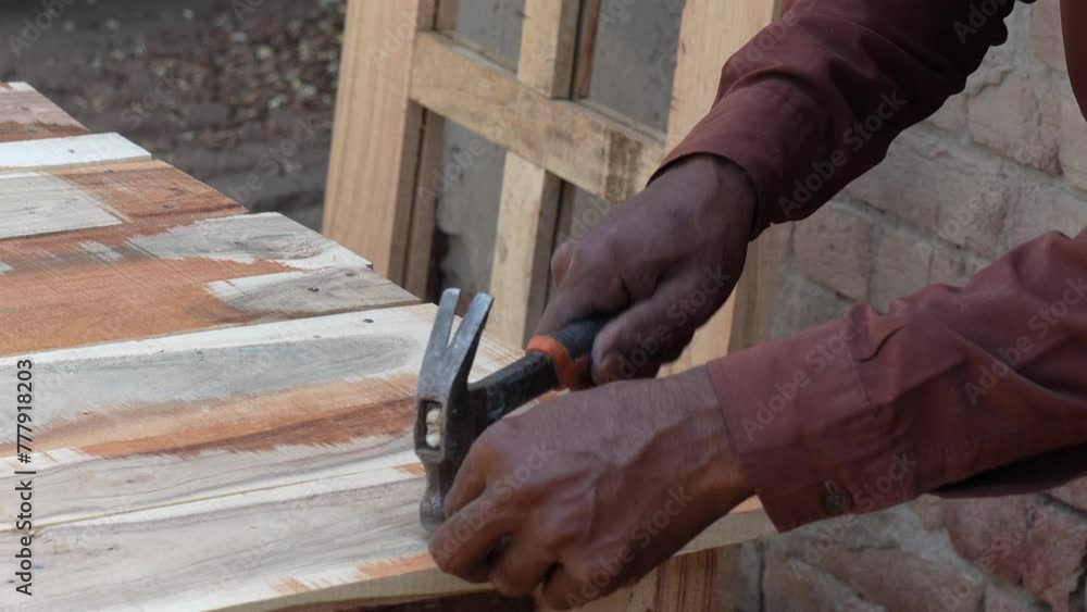worker hands nailing nails to the soft surface of a wooden block using ...