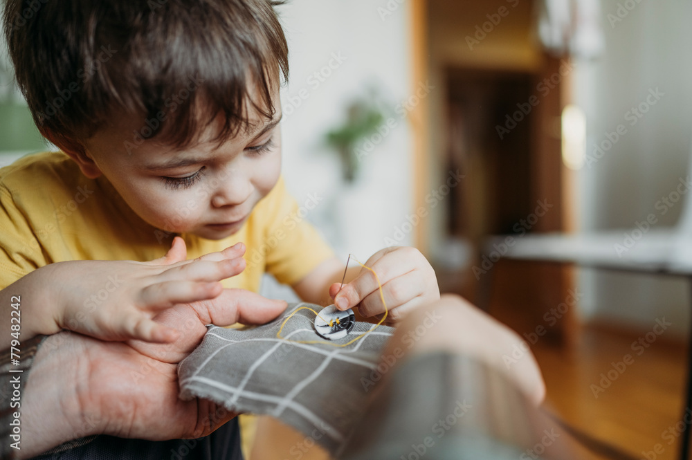 Father teaching son to sew button on gray colored cloth Stock Photo ...