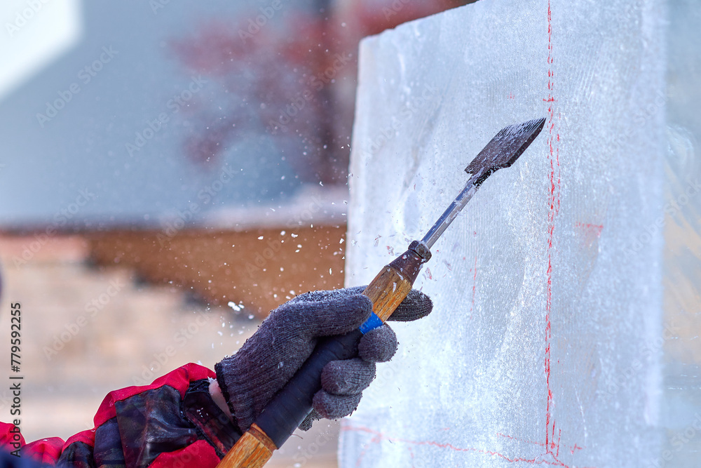 A sculptor processes a large ice cube with a sharp hand tool. Ice dust ...