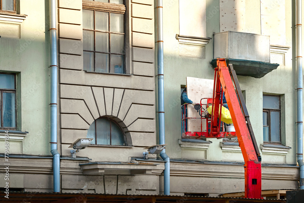 Workers in crane bucket board up window before reconstruction work ...