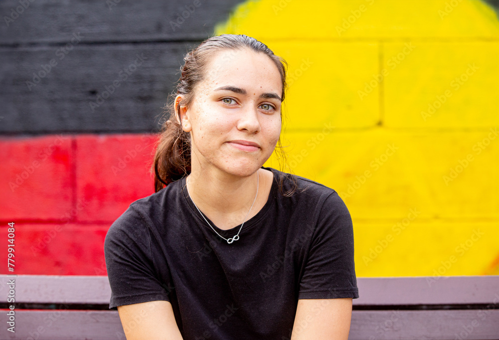 Portrait of an Aboriginal woman sitting in front of a painted wall ...