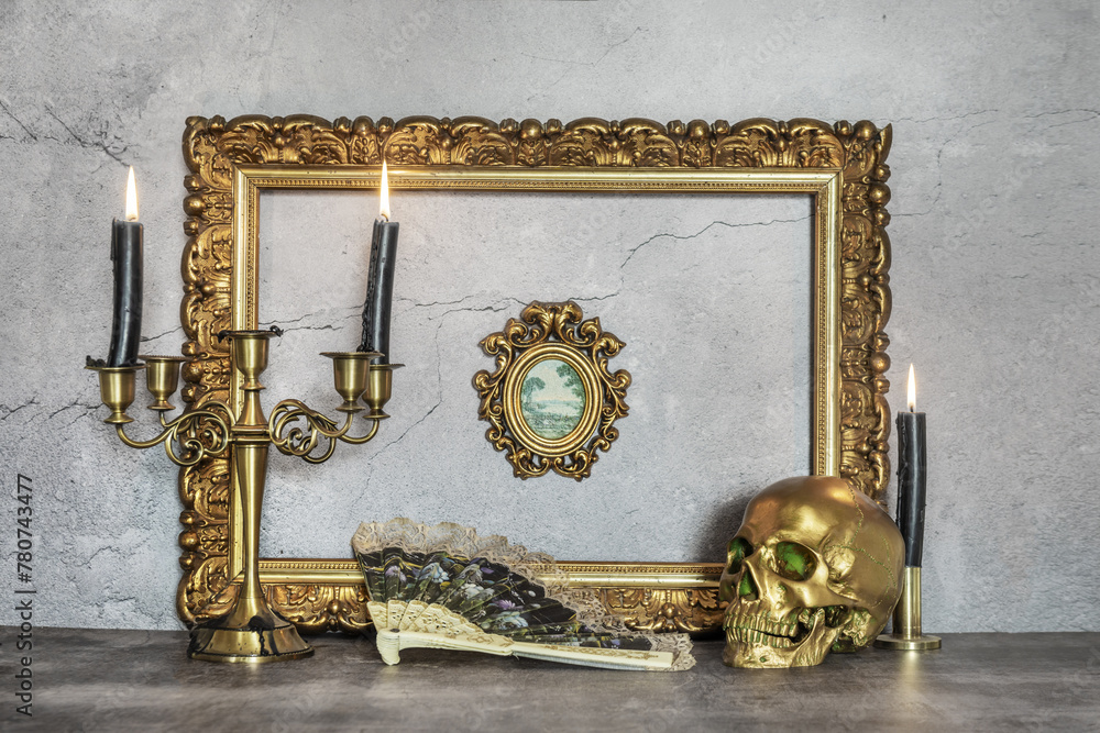 A decorative still life with a golden frame next to a golden skull next ...