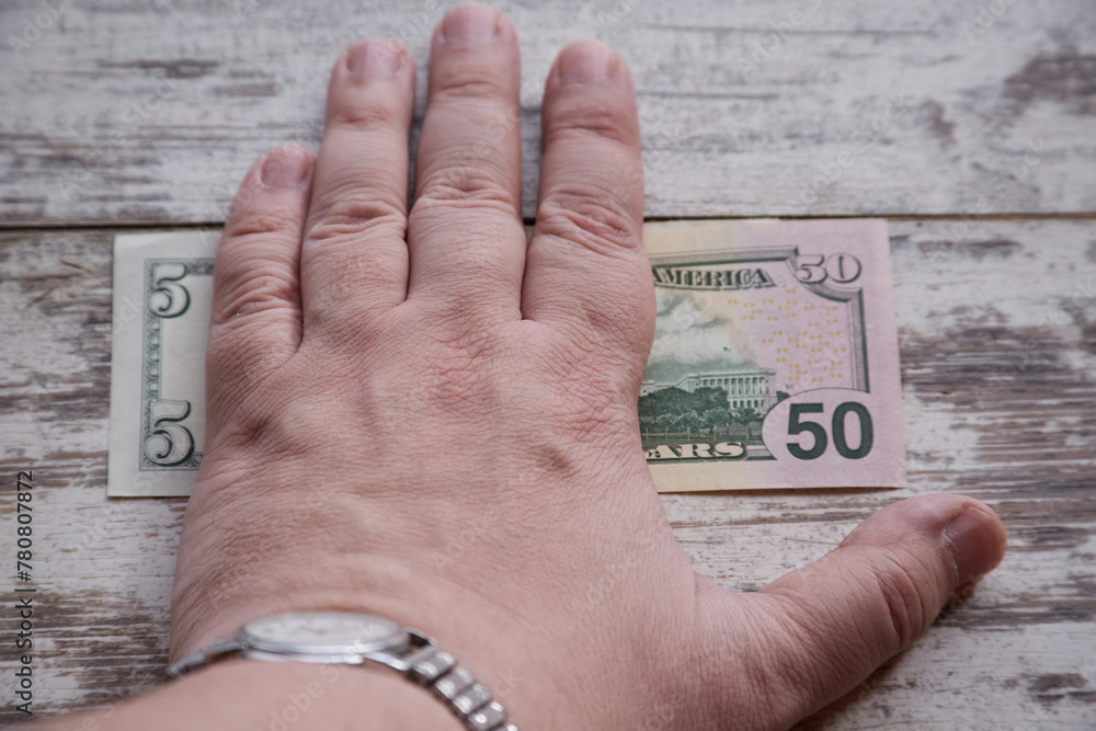 A hand covers five-dollar and fifty-dollar bills on a worn empty table ...