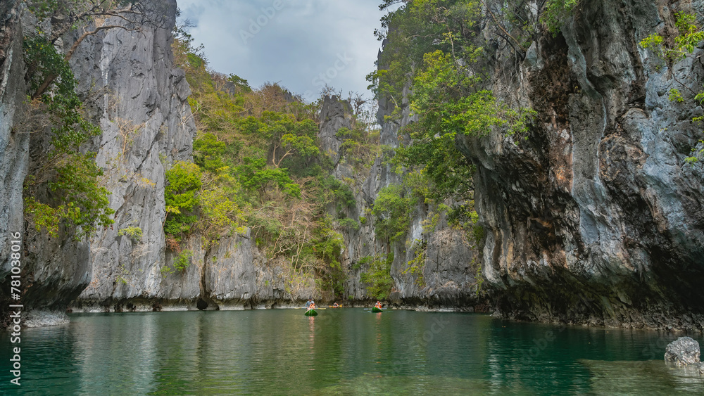 Canoes with tourists sail along a calm emerald lagoon surrounded by ...