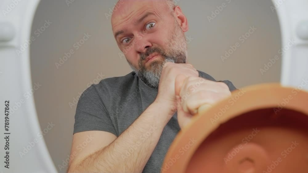Funny bald man plumber cleaning toilet with plunger. Male plumber using ...