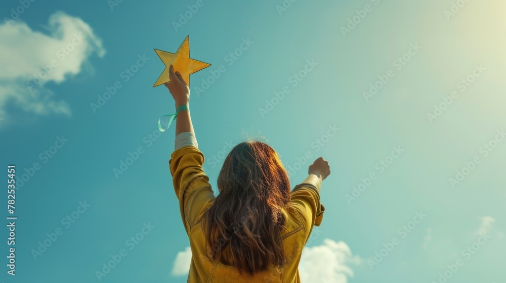 Closeup a woman hand raised while holding gold star at blue sky ...
