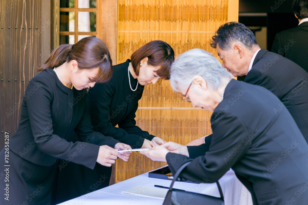 お葬式・告別式・お通夜の受付で香典を渡す高齢者の遺族・弔問客と葬祭ディレクター Stock Photo | Adobe Stock
