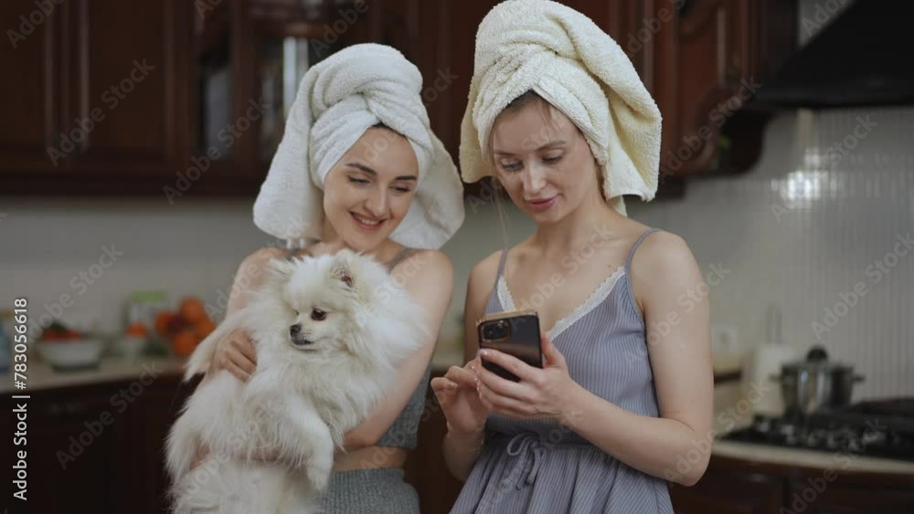 Two young women with towels on their heads look at a mobile phone ...