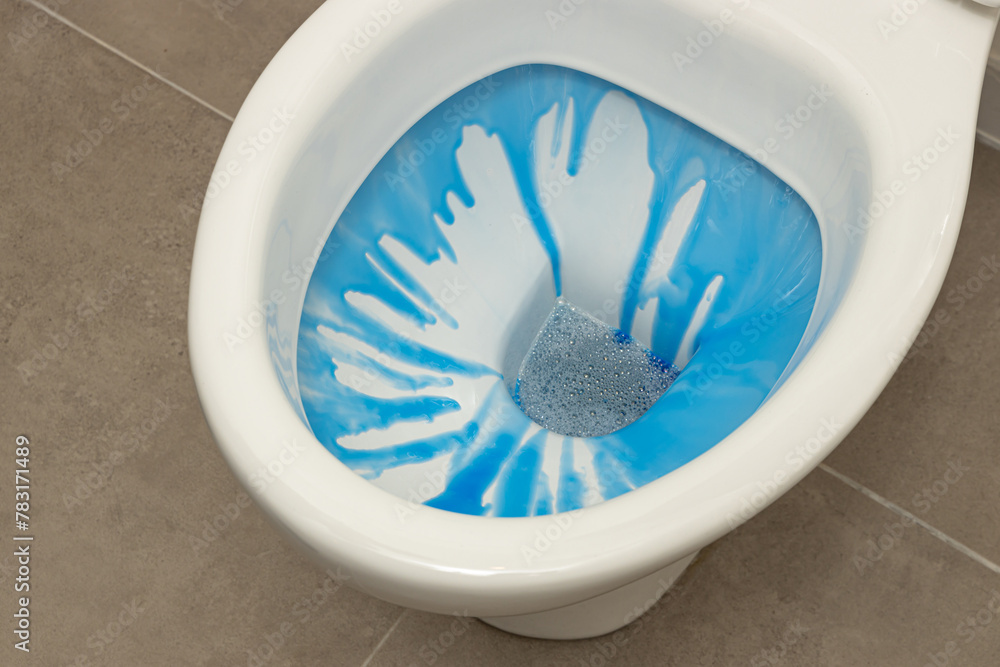 Close up concept shot of a toilet bowl with blue toilet cleaner running ...