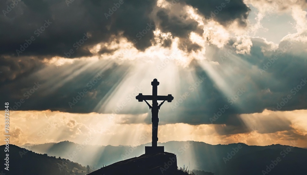 silhouette of crucifix against dramatic cloudy sky with beams of sunlight sun rays breaking ...