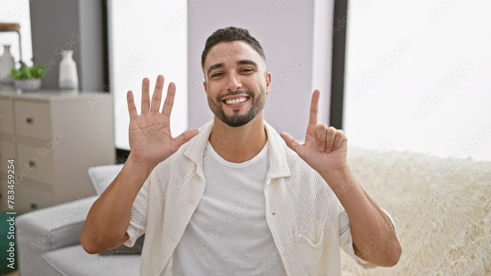 Cheerful young arab man at home, casually sitting on his living room ...