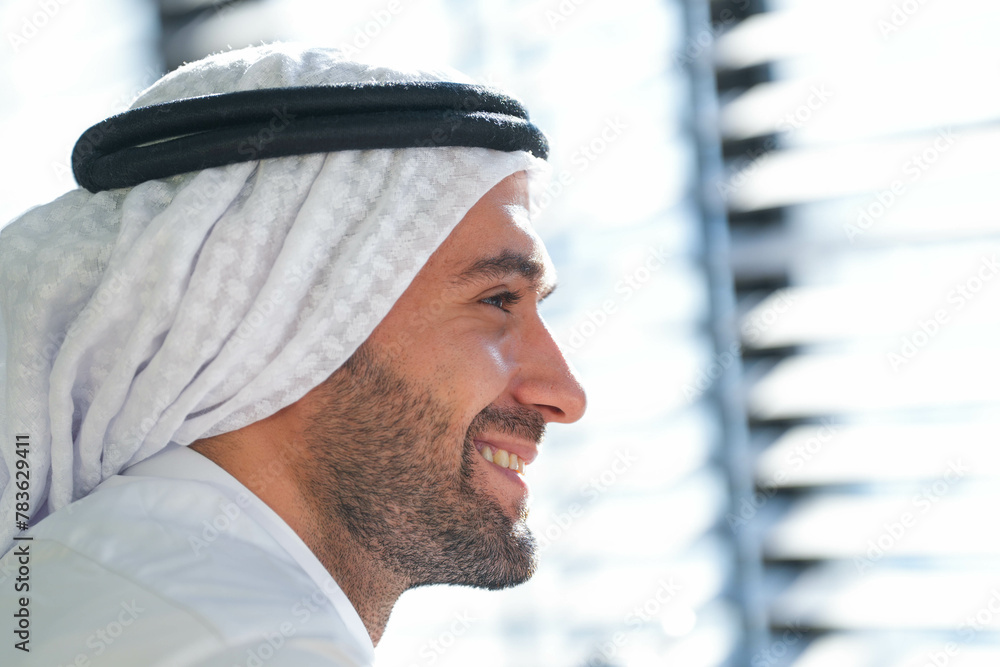 Profile of a smiling man in traditional Emirati attire, his face lit by ...