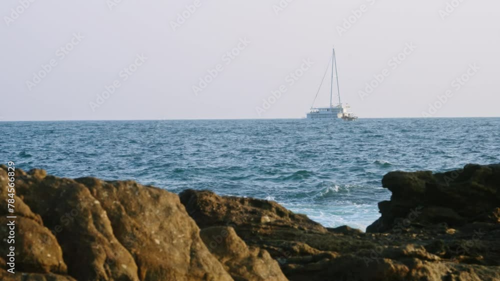 Luxury yacht sails on open ocean, visible from rugged coastline ...