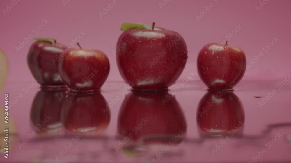 Three red apples displayed on a pink surface, one in water and one in a ...