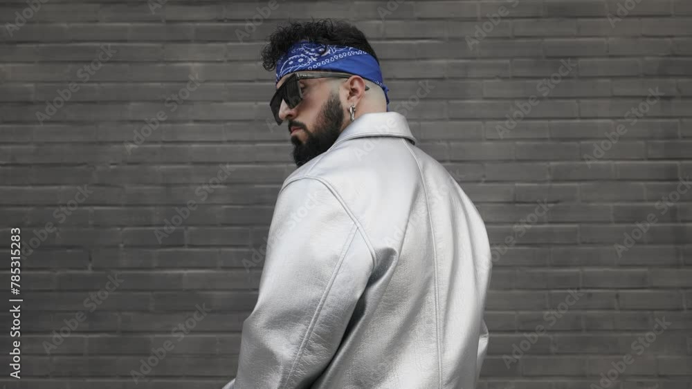 Stylish bearded man in streetwear turning to glance at the camera over ...