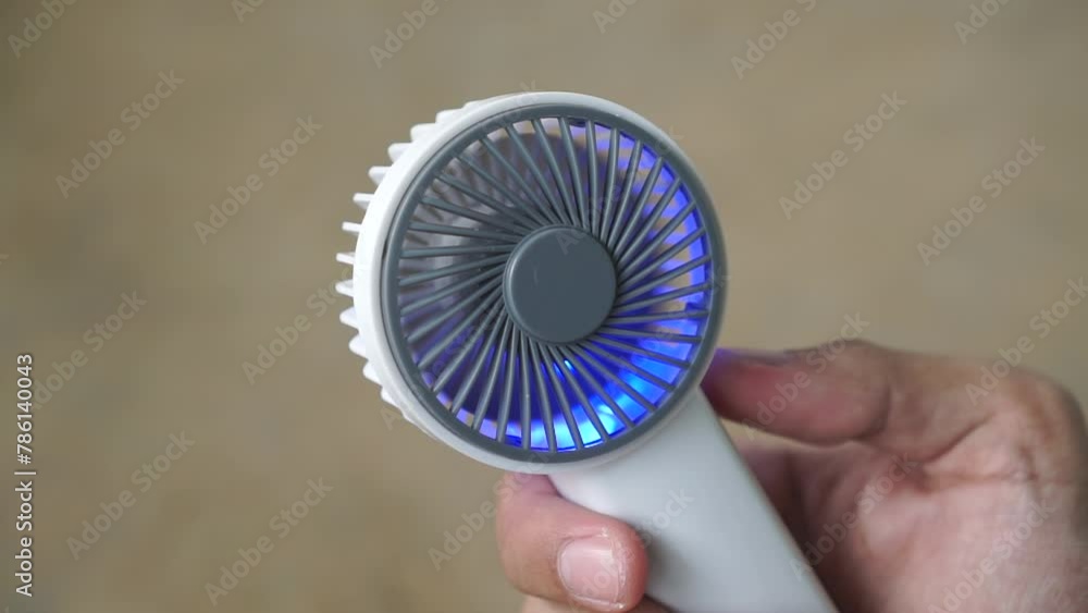 A mini hand electric fan is spinning with the outdoor background. Stock ...