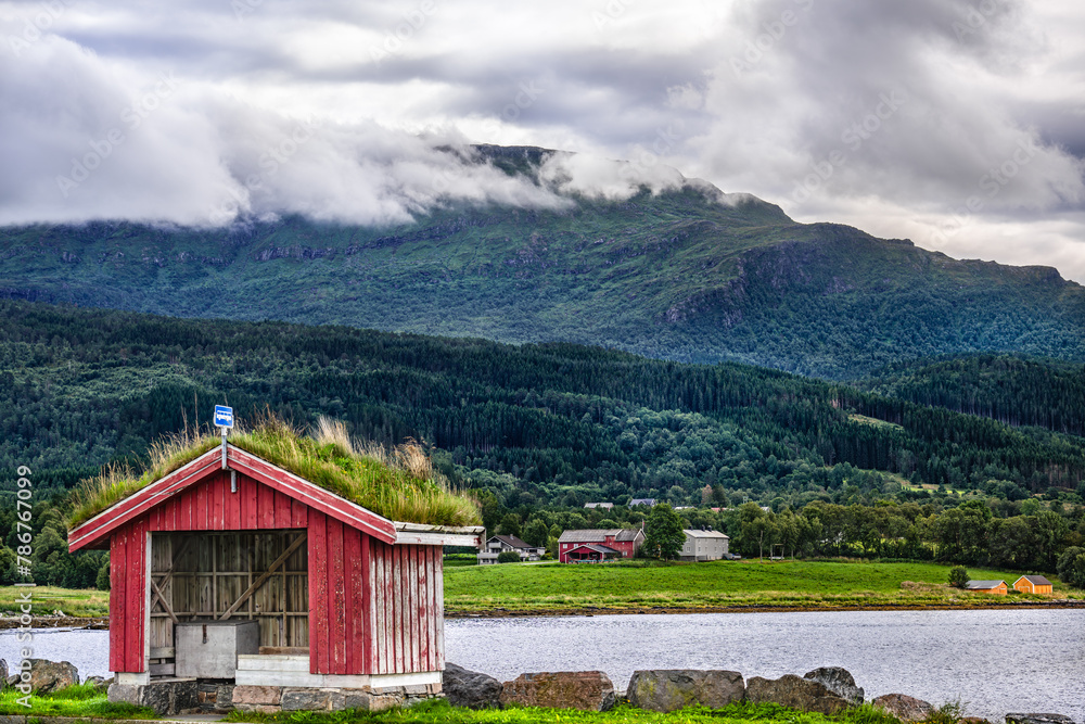 A quaint red bus shelter with a lush green sod roof stands by ...