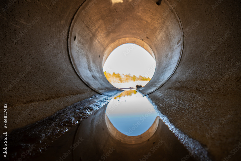 Poster Inside a circular concrete drainage culvert with a trickle of ...
