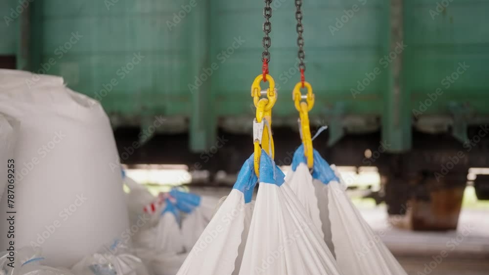 Industrial crane hooks lifting heavy white bags in a warehouse. Factory ...