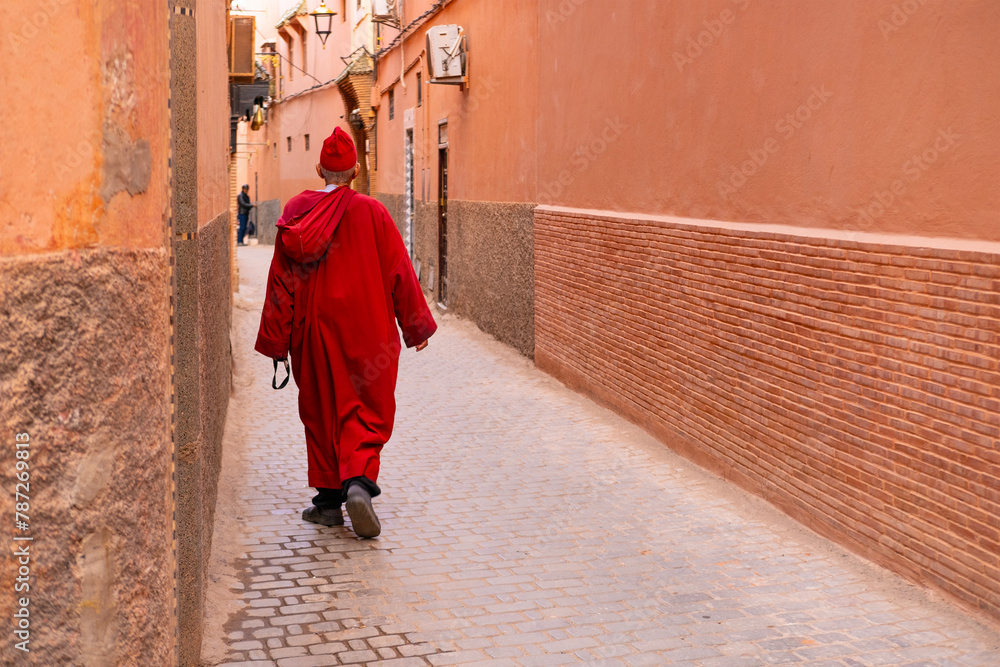 man in traditional long attire walks down street along high wall Red ...