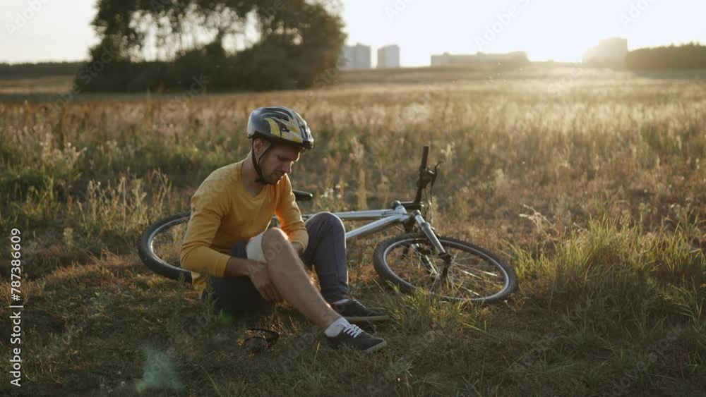 Sad white man bandaging knee after falling from bicycle. First aid for ...