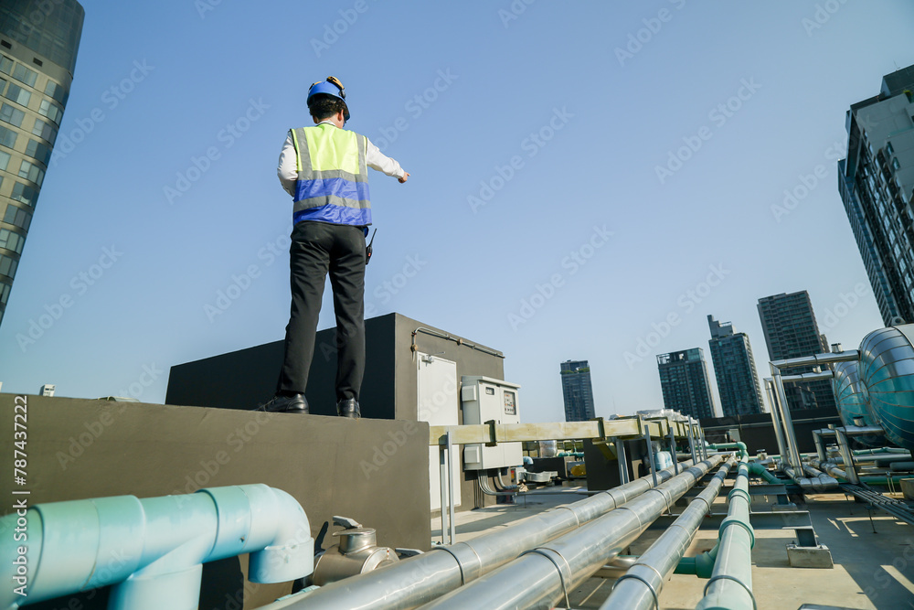 Engineer with tablet on rooftop assessing HVAC system against city ...