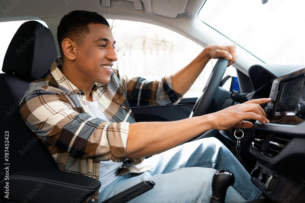 Road playlist. Happy black man driving car and checking automobile ...