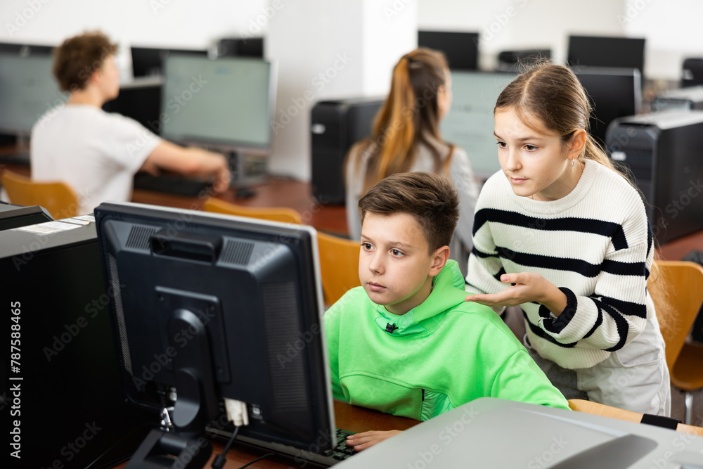 Schoolboy helping girl, his classmate, to find solution of computer ...