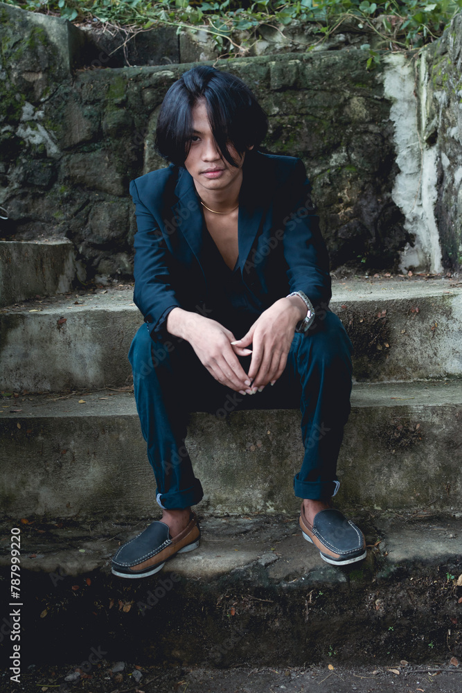 Young Asian man in goth-inspired attire sitting solemnly in a forest ...
