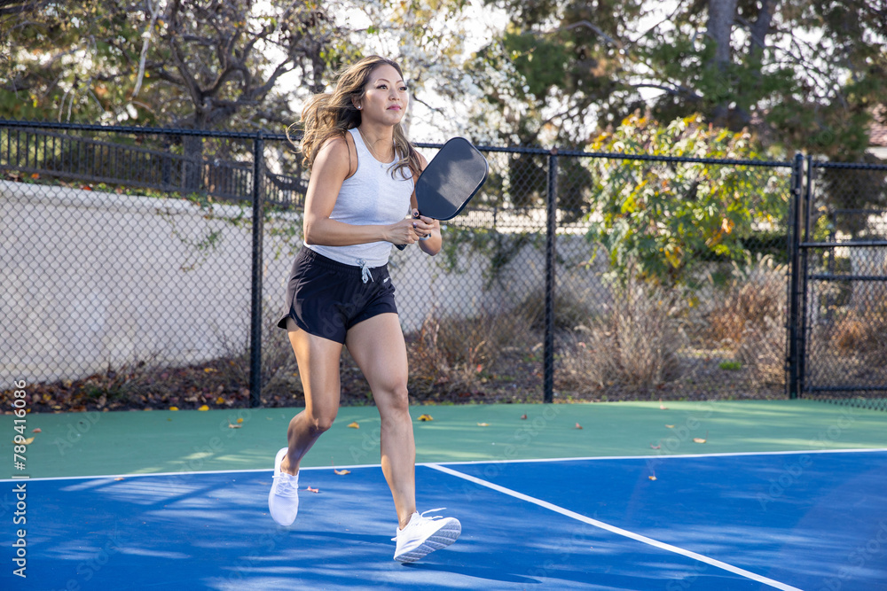 Asian woman playing pickleball on a court with her paddle outside. The ...