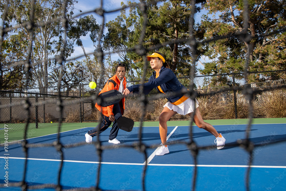 Mixed race couple playing a game of pickleball together outside on a ...