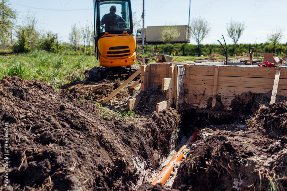 Excavator digging trench in soil for sewage pipeline during building ...