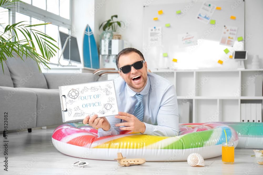 Happy male office worker on inflatable ring holding sign with text OUT ...