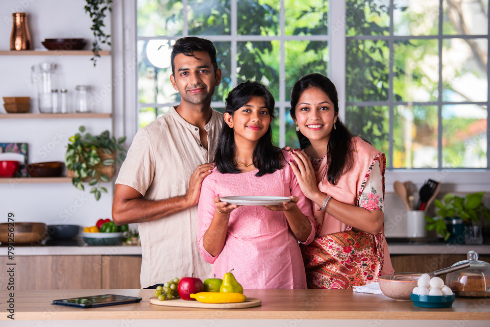 Cute little indian master chef with young parents in the kitchen making ...