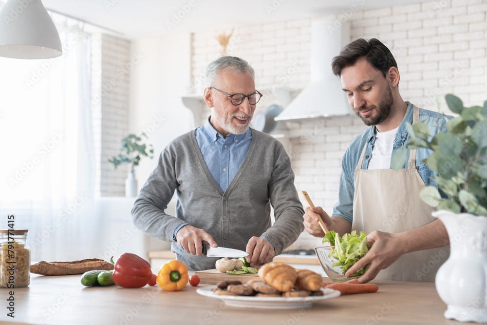 Elderly senior old father helping his young adult son in cooking lunch ...