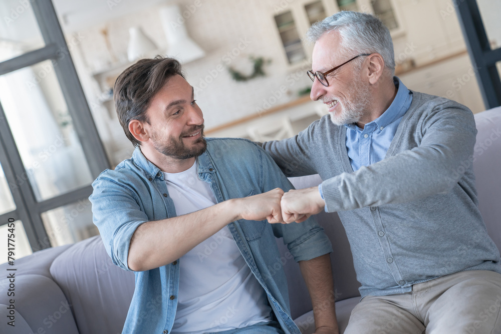 Old elderly senior father together with his young adult son doing fists gesture, giving fists ...