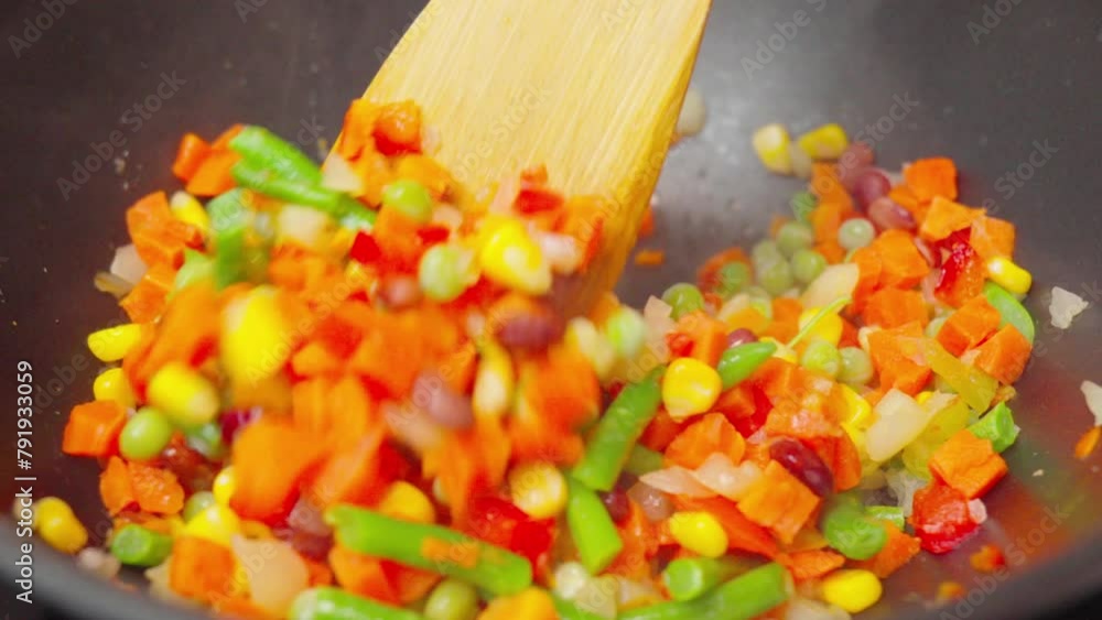 Colorful chopped vegetables is being stirred using a wooden spoon. The ...