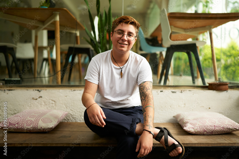 Smiling Gen Z transgender office worker in smart casual clothes sits on ...