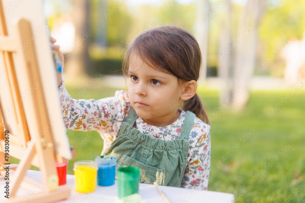 Little girl is painting a picture in the park on the green grass. Child ...